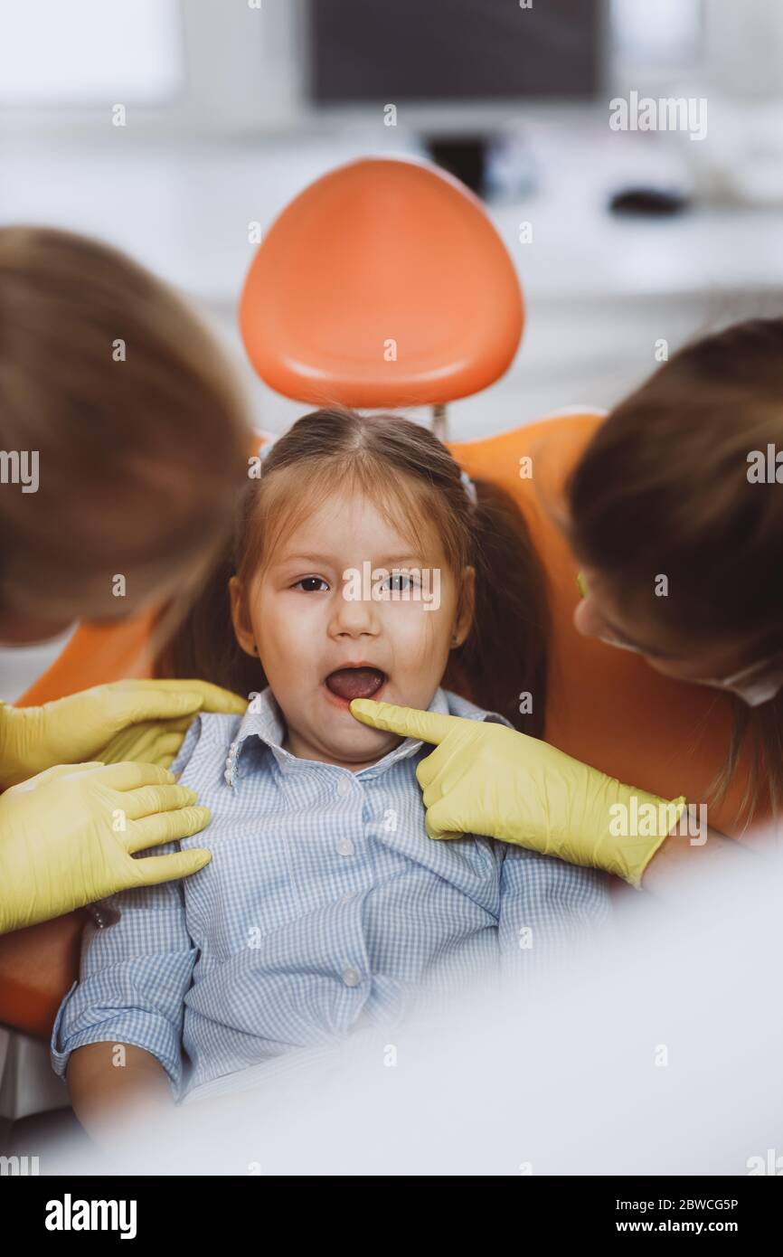 Crop female dentists in yellow gloves examining teeth of little patient ...