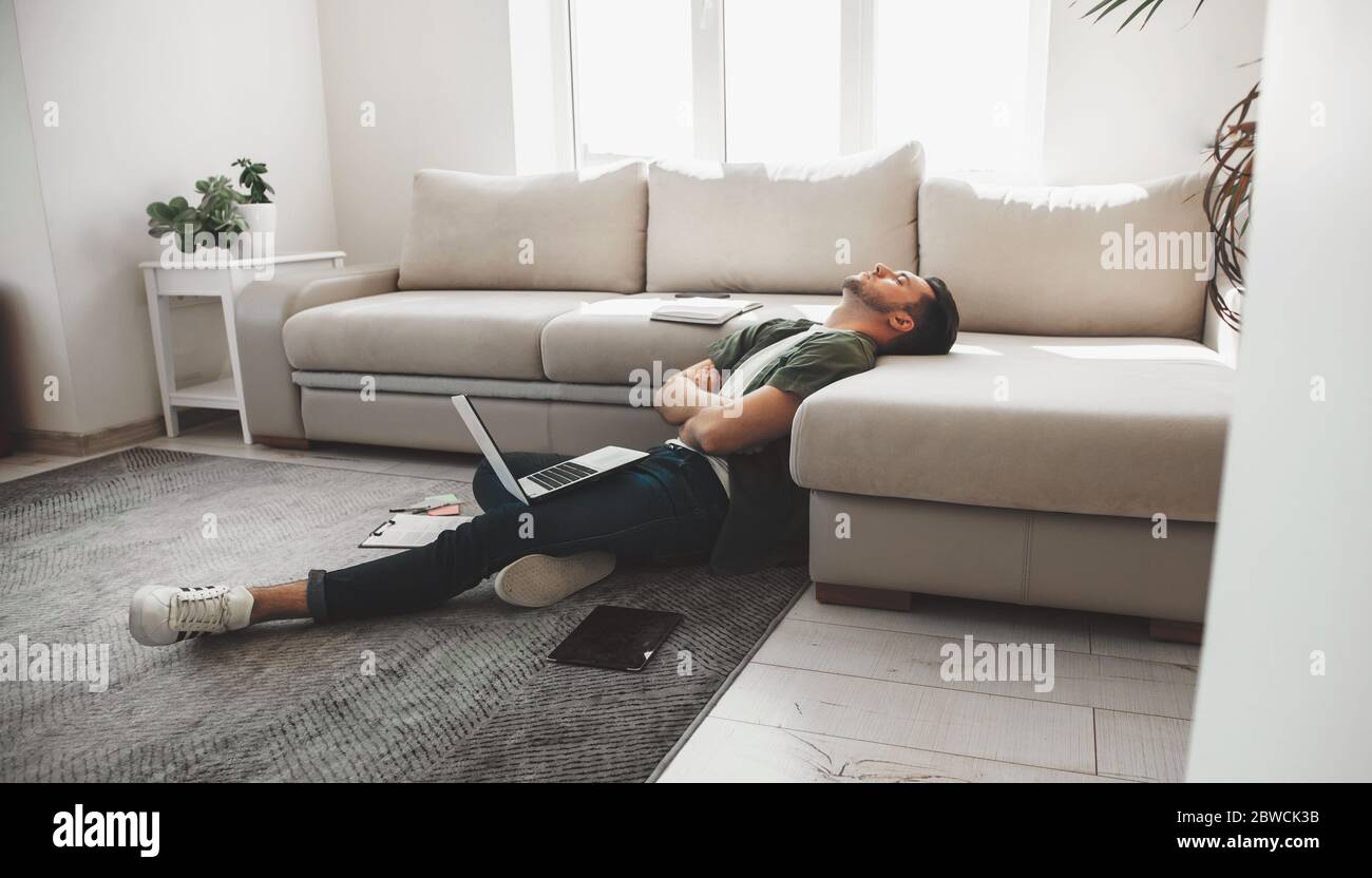 Tired caucasian man falling asleep on the floor with a computer and ...