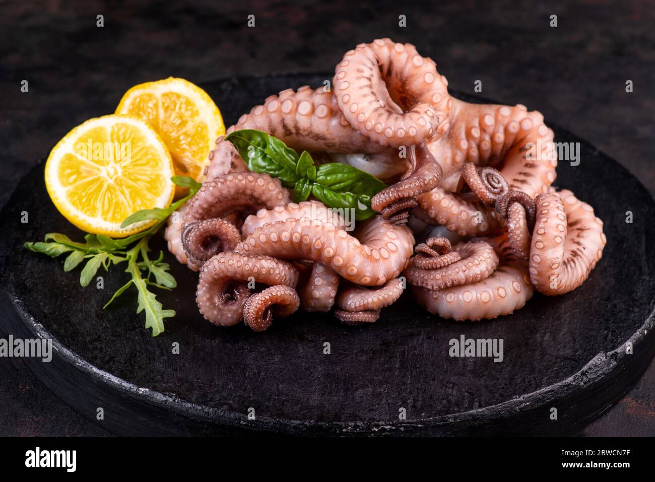Sea food.Raw octopus tentacles on a black round plate on a black ...