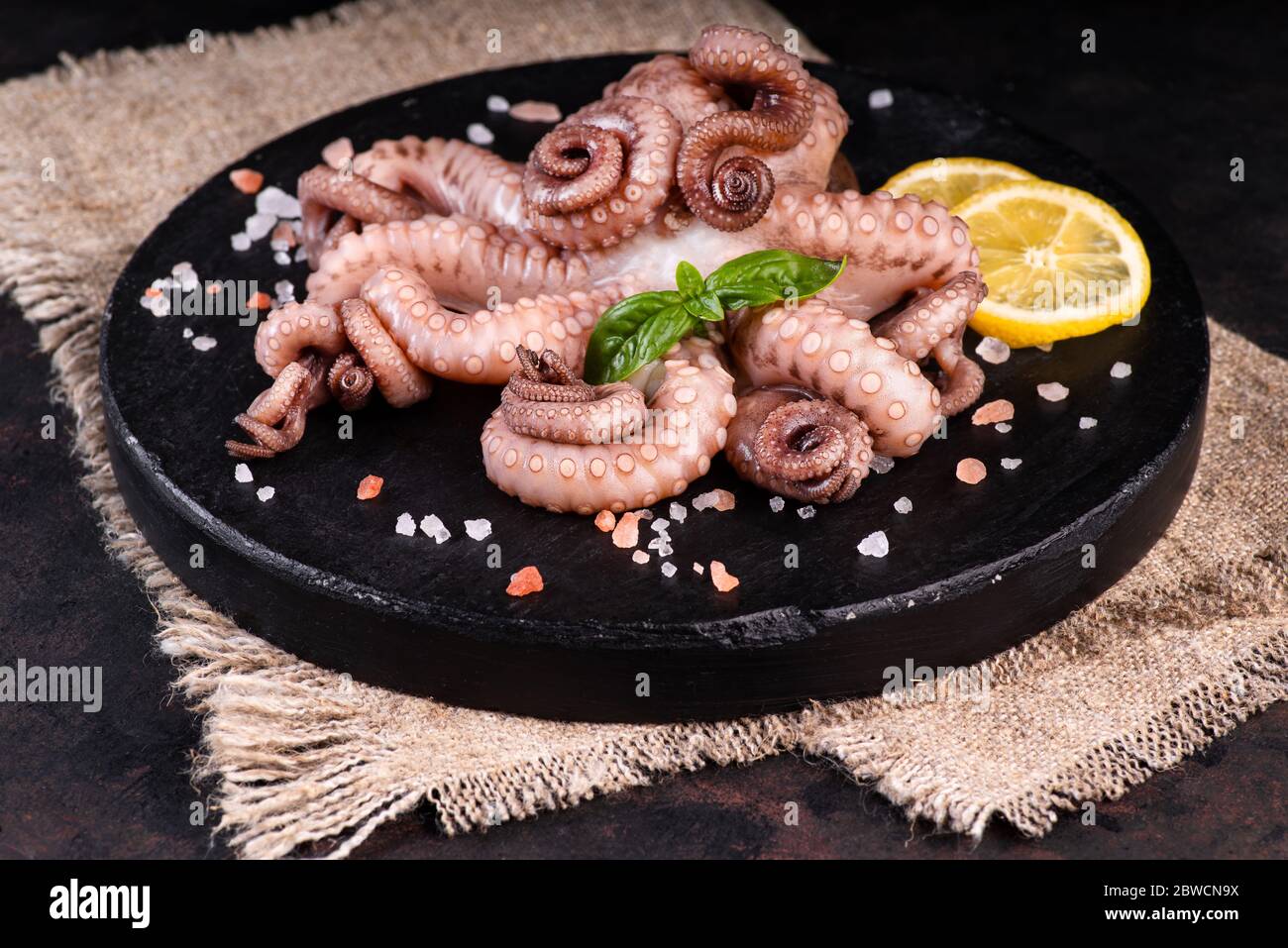 Sea food.Raw octopus tentacles on a black round plate on a black ...