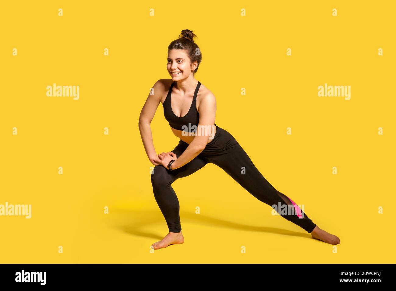 Happy athletic girl with hair bun in tight sportswear doing lower body ...