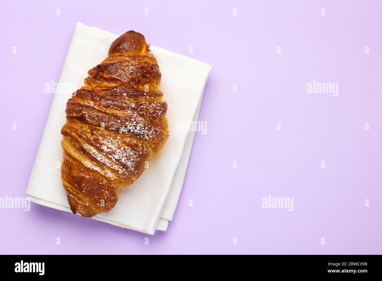 Freshly baked croissant with sugar powder on a purple background with ...