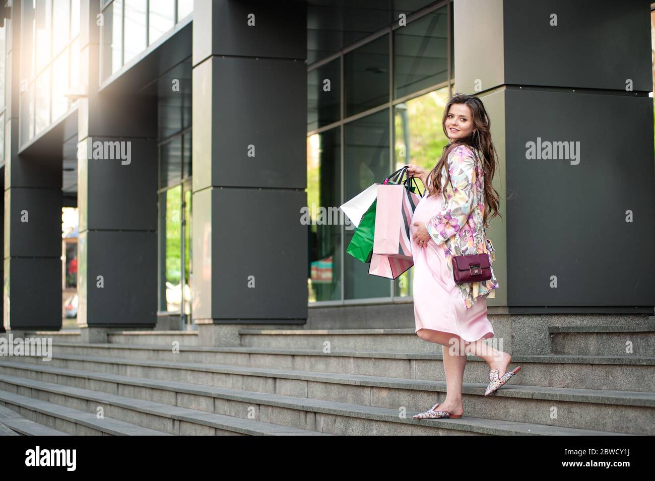 A pregnant woman walking with packages near a shopping center Stock ...
