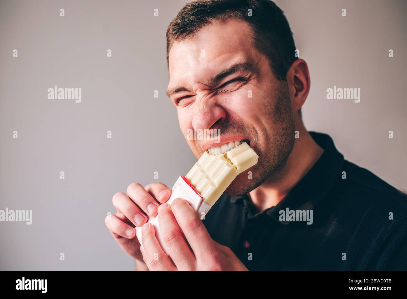 Young man isolated over background. Guy biting chocolate with ...