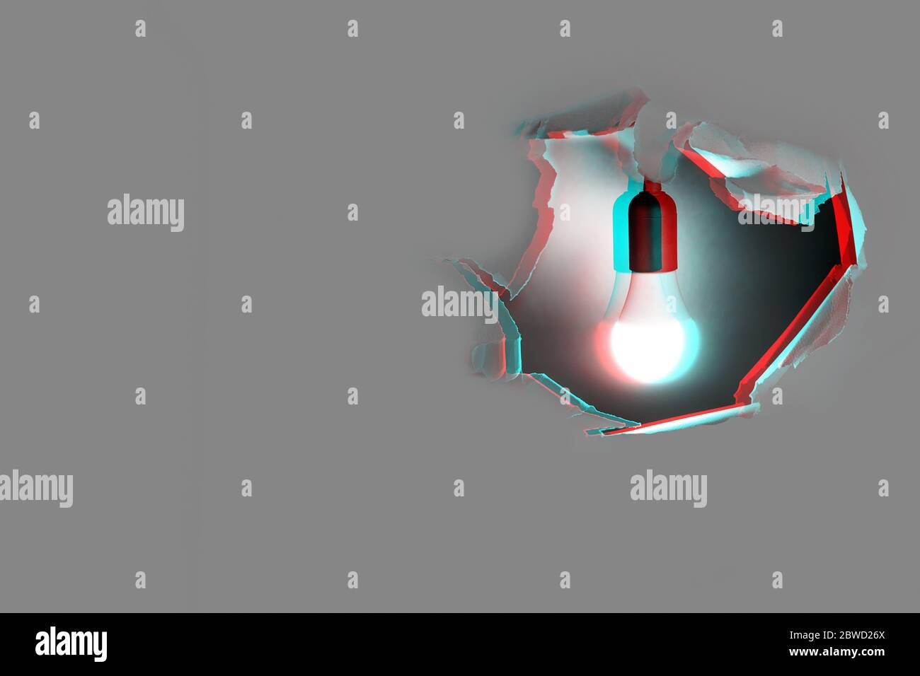 Concept of creative idea. A light bulb shines in a hole of gray paper ...