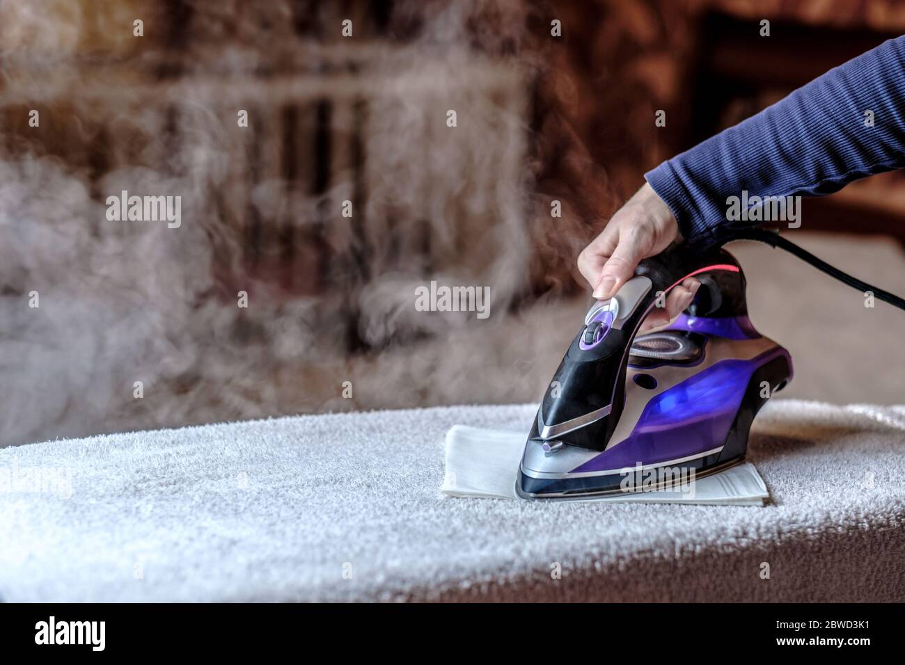 Closeup female hand ironing clothes on the table. Puffs of hot steam ...