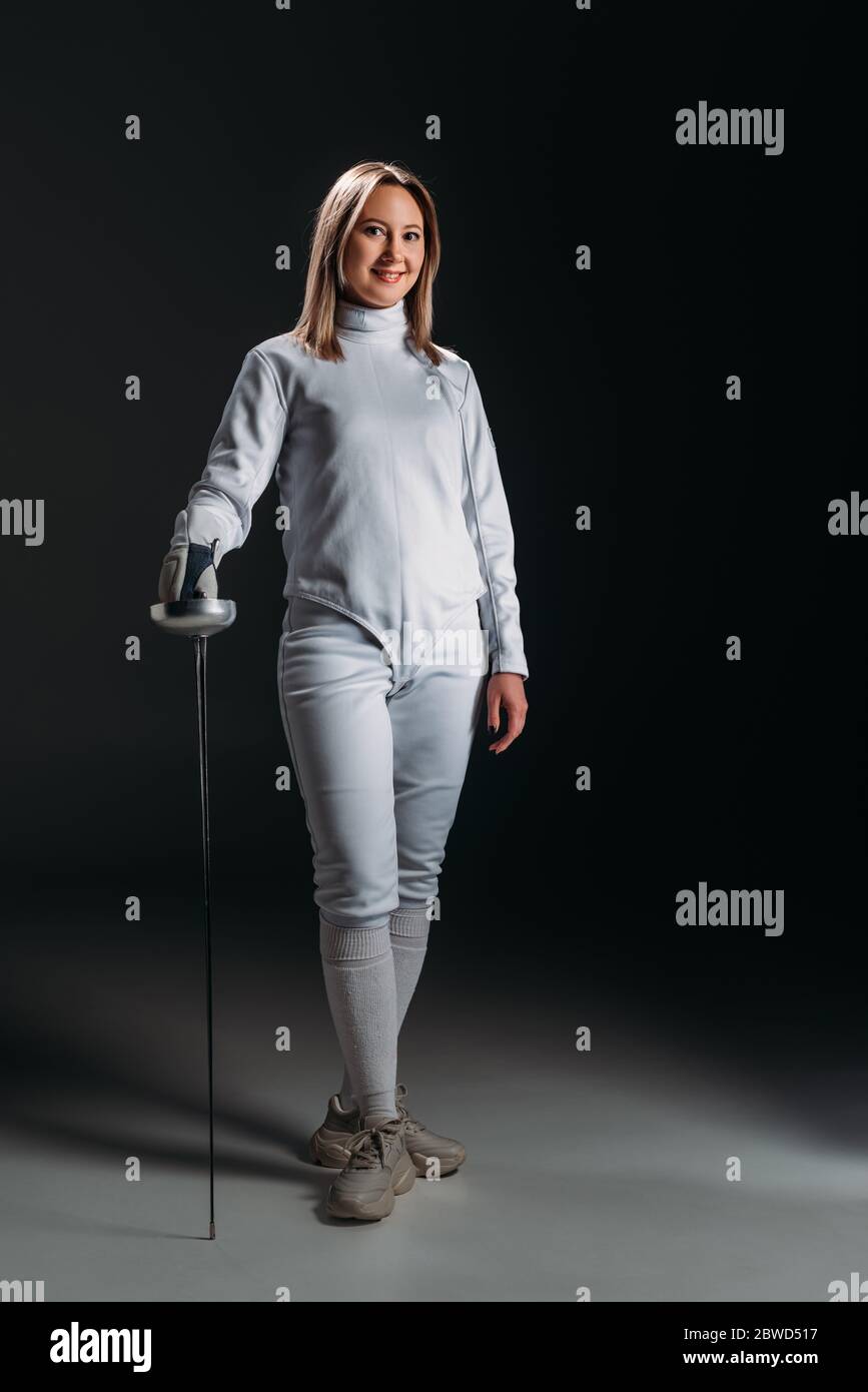 Smiling fencer in fencing suit and glove looking at camera while ...