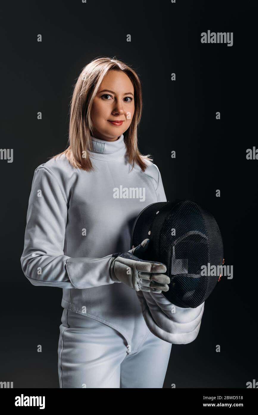 Attractive fencer in fencing suit holding mask and looking at camera ...