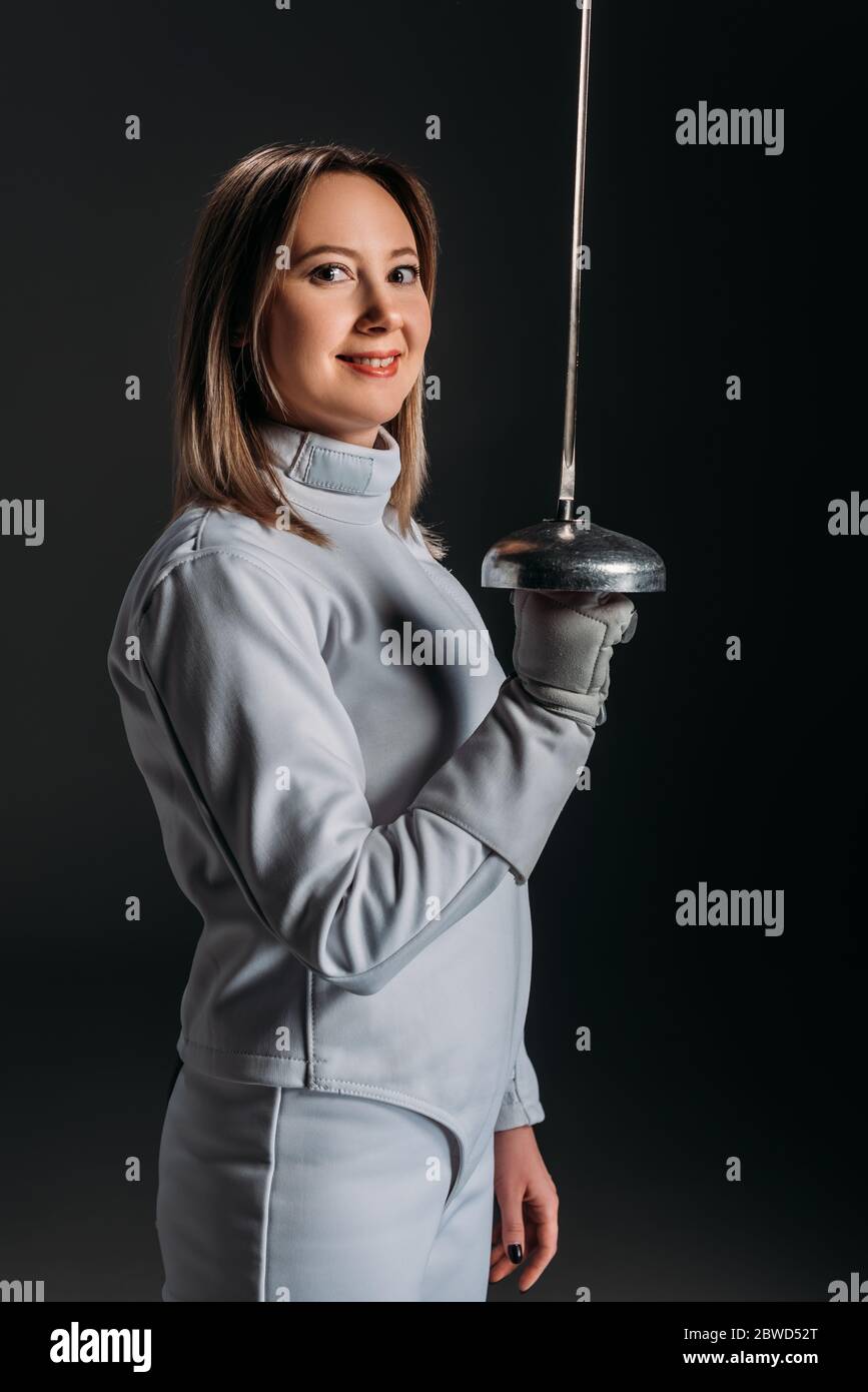 Side view of beautiful fencer smiling at camera while holding rapier ...