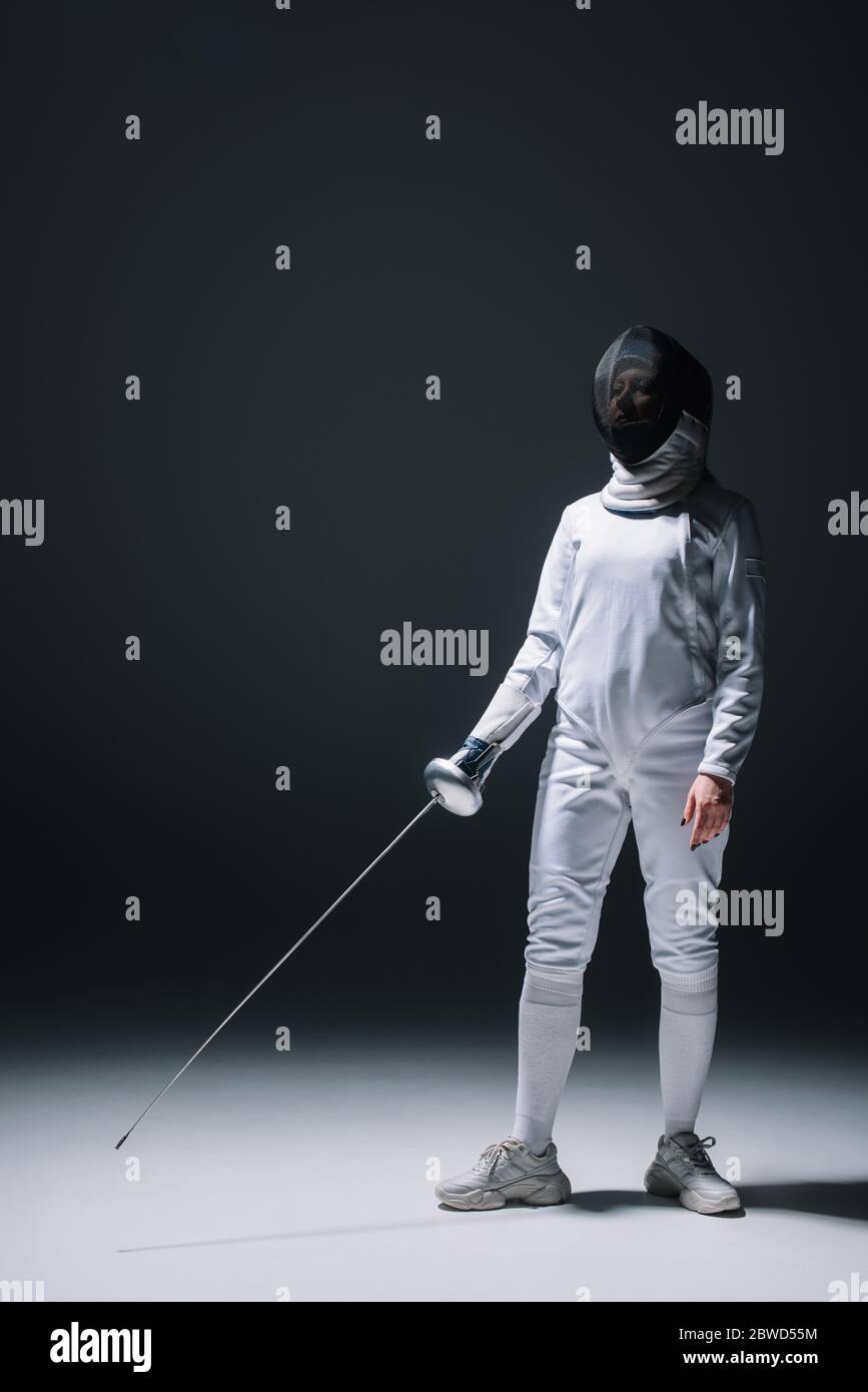 Fencer in fencing mask holding rapier while standing on white surface ...