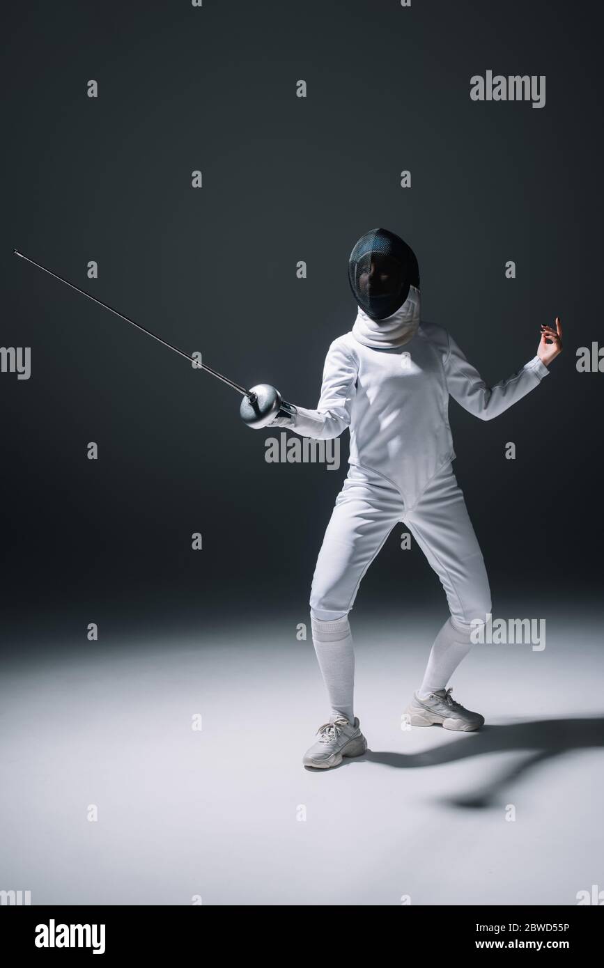 Fencer in fencing mask training with rapier on white surface on black ...