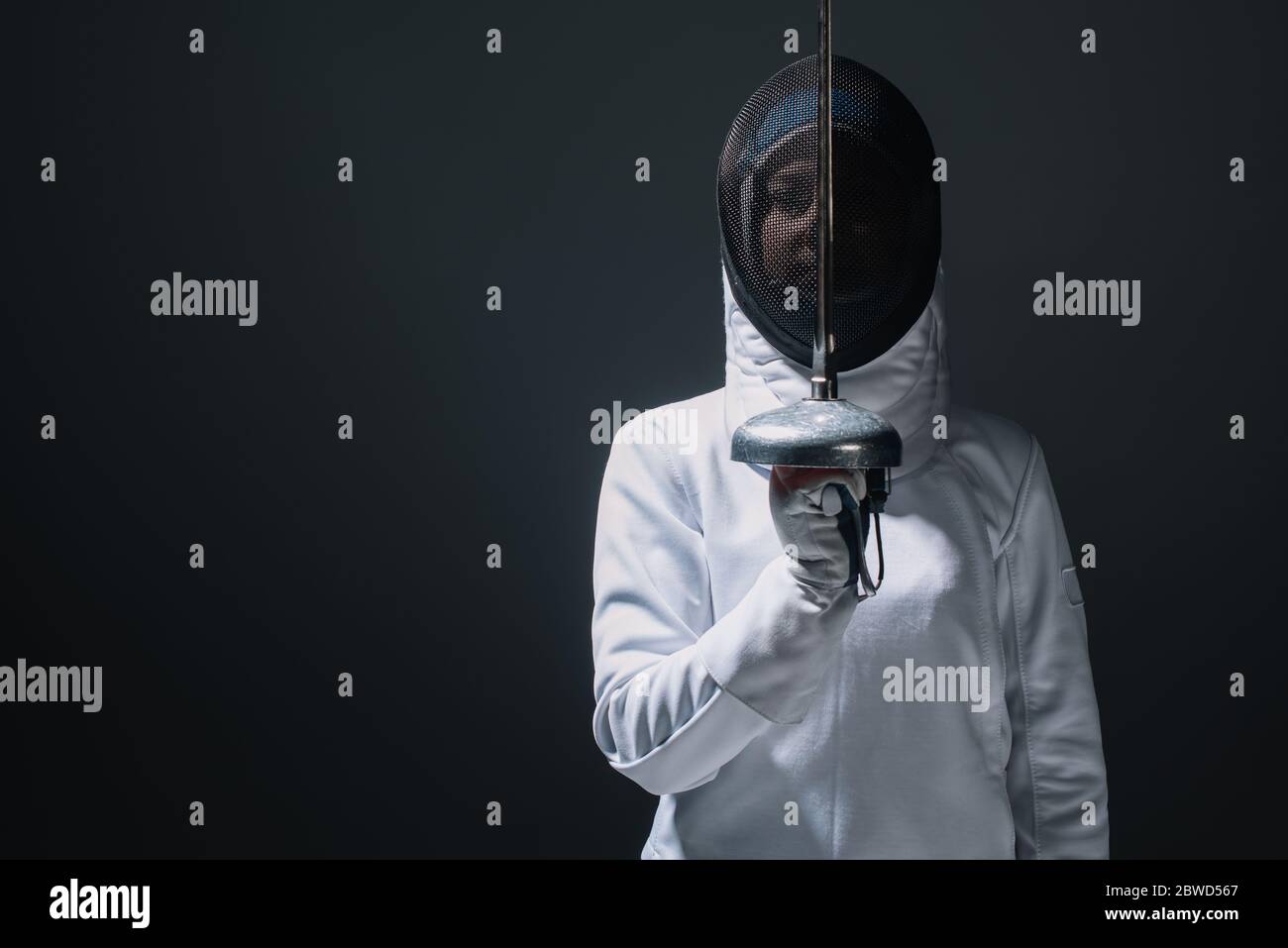 Fencer holding rapier near fencing mask isolated on black Stock Photo ...