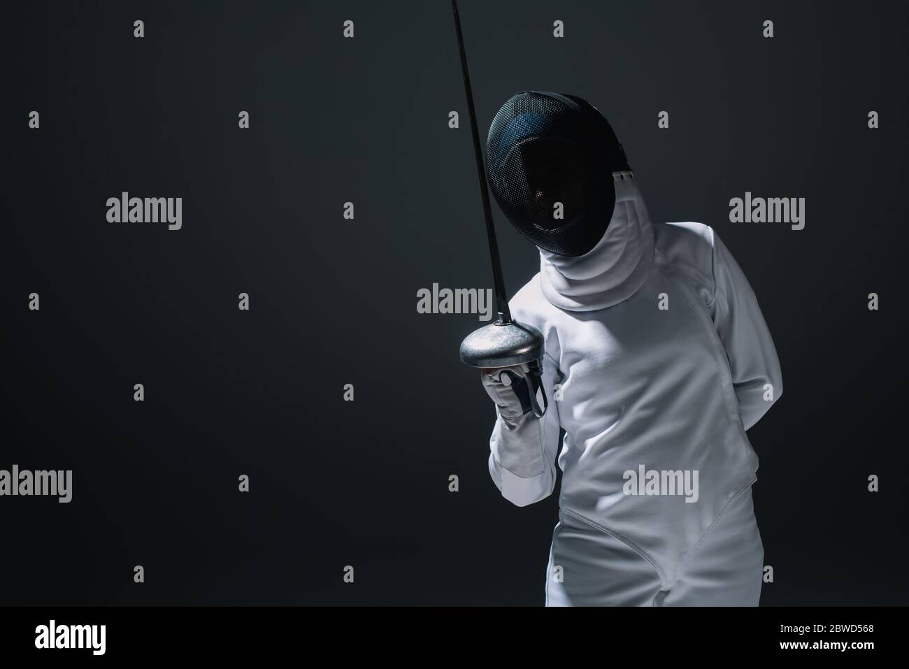 Swordswoman in fencing suit and mask holding rapier isolated on black ...