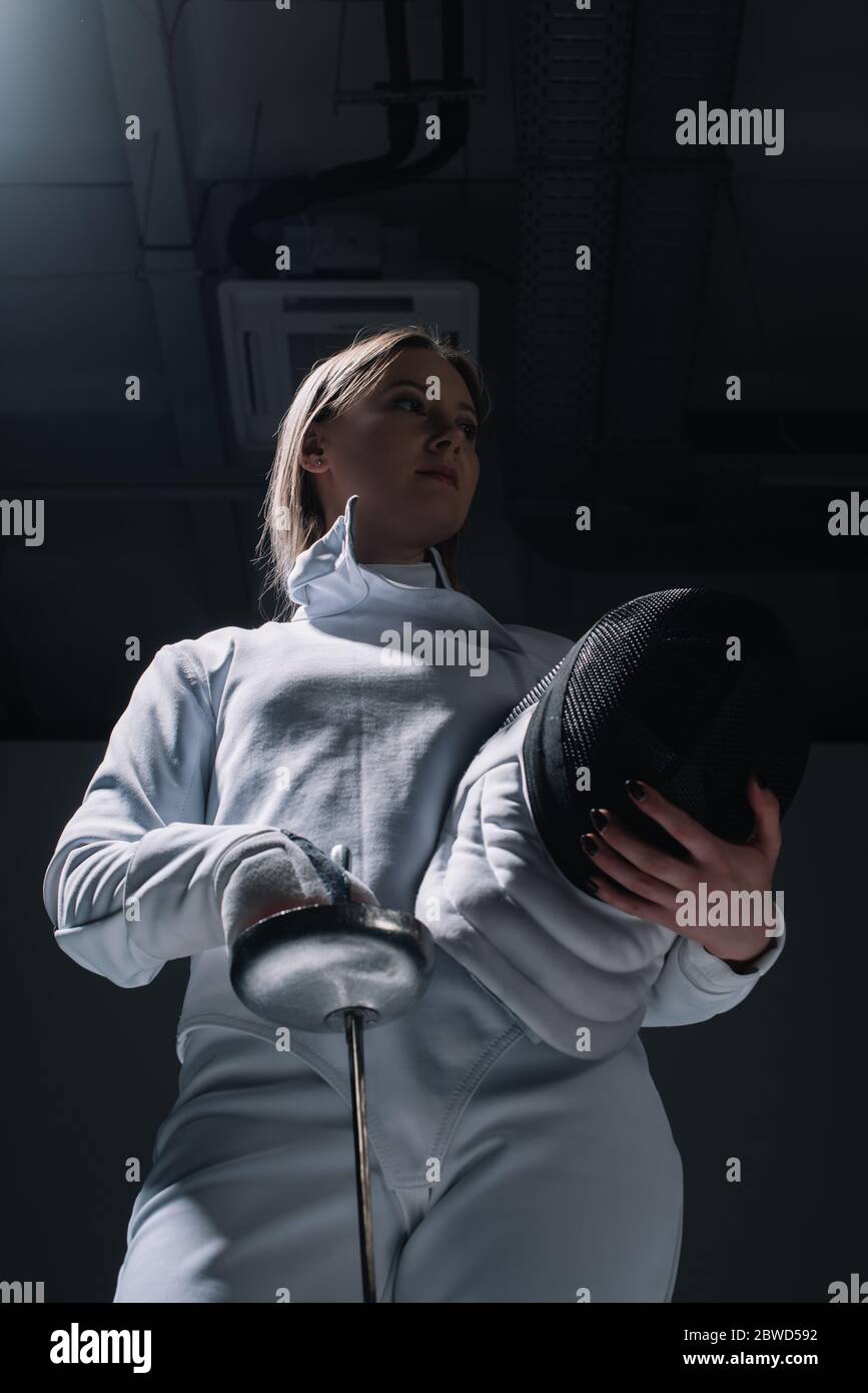 Low angle view of beautiful fencer holding rapier and fencing mask ...