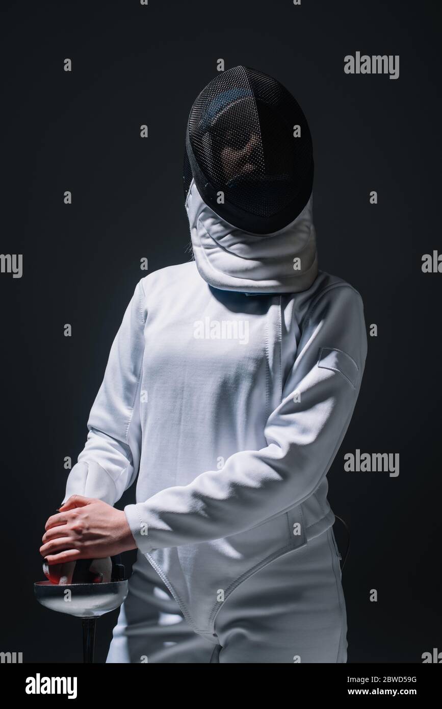 Fencer in fencing suit and mask holding rapier isolated on black Stock ...
