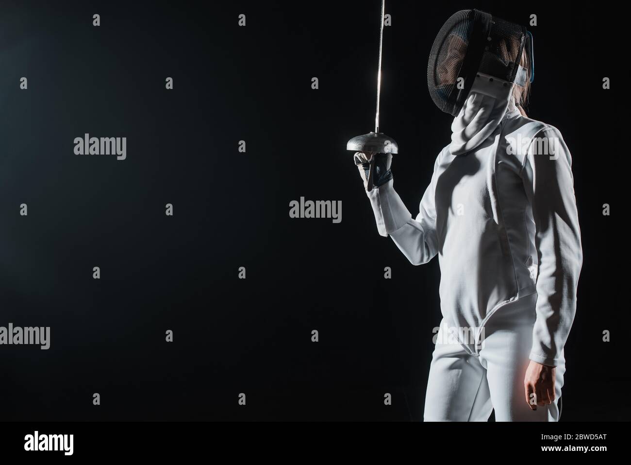 Fencer in fencing mask and suit holding rapier isolated on black Stock ...