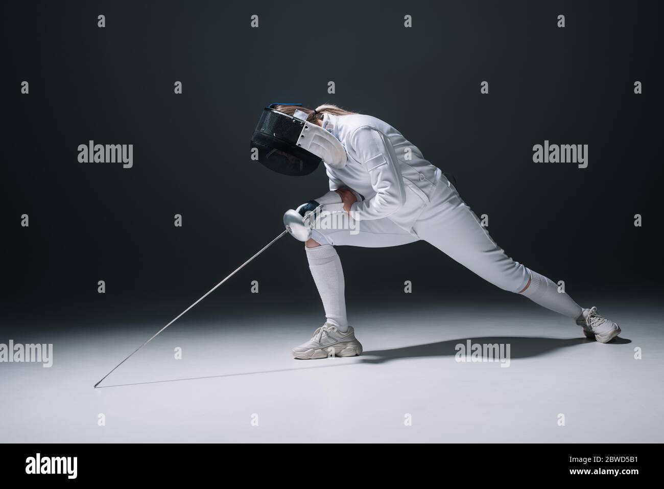 Fencer doing lunge while holding rapier on white surface on black ...