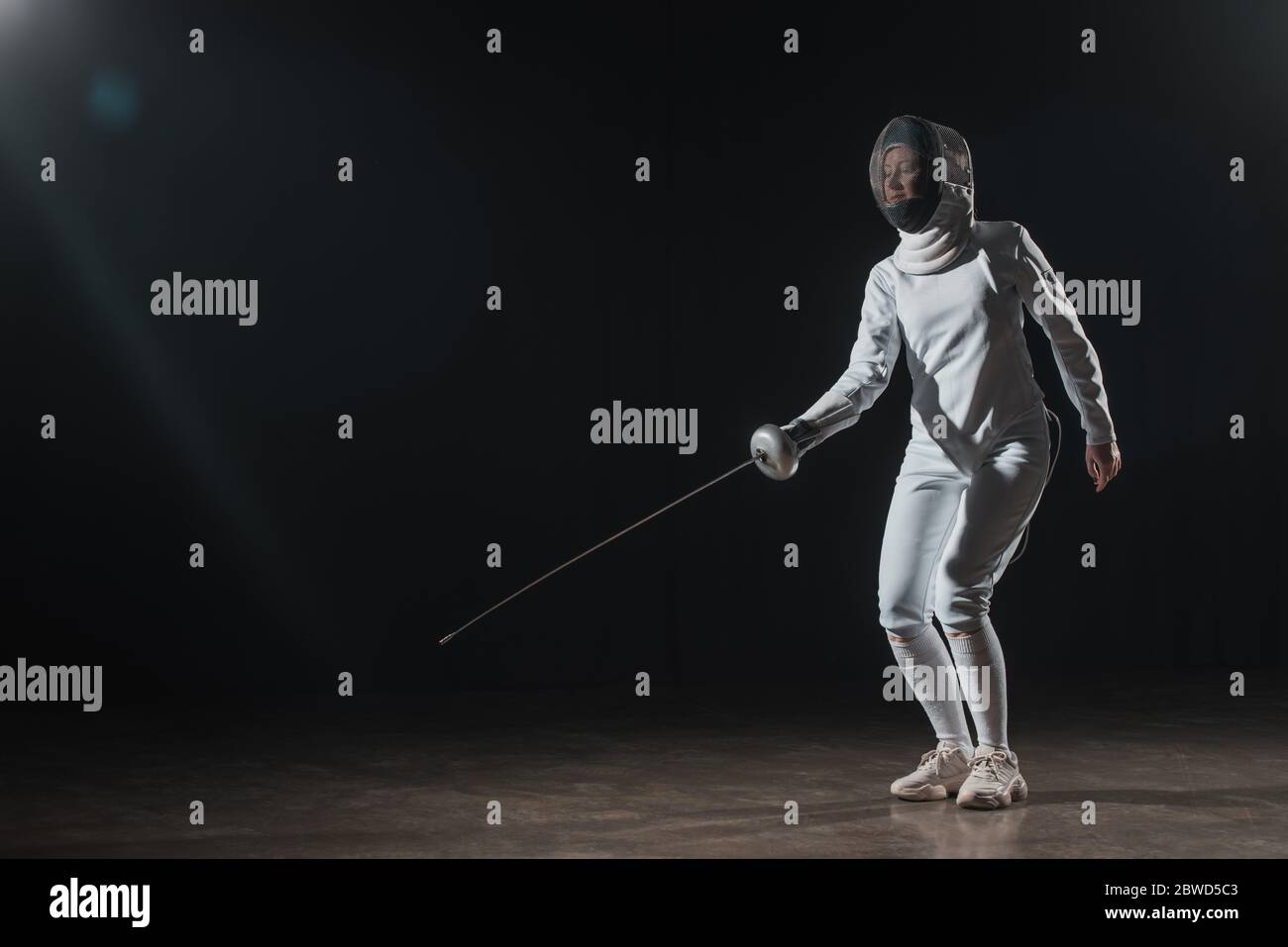 Swordswoman in fencing mask and suit training with rapier under ...