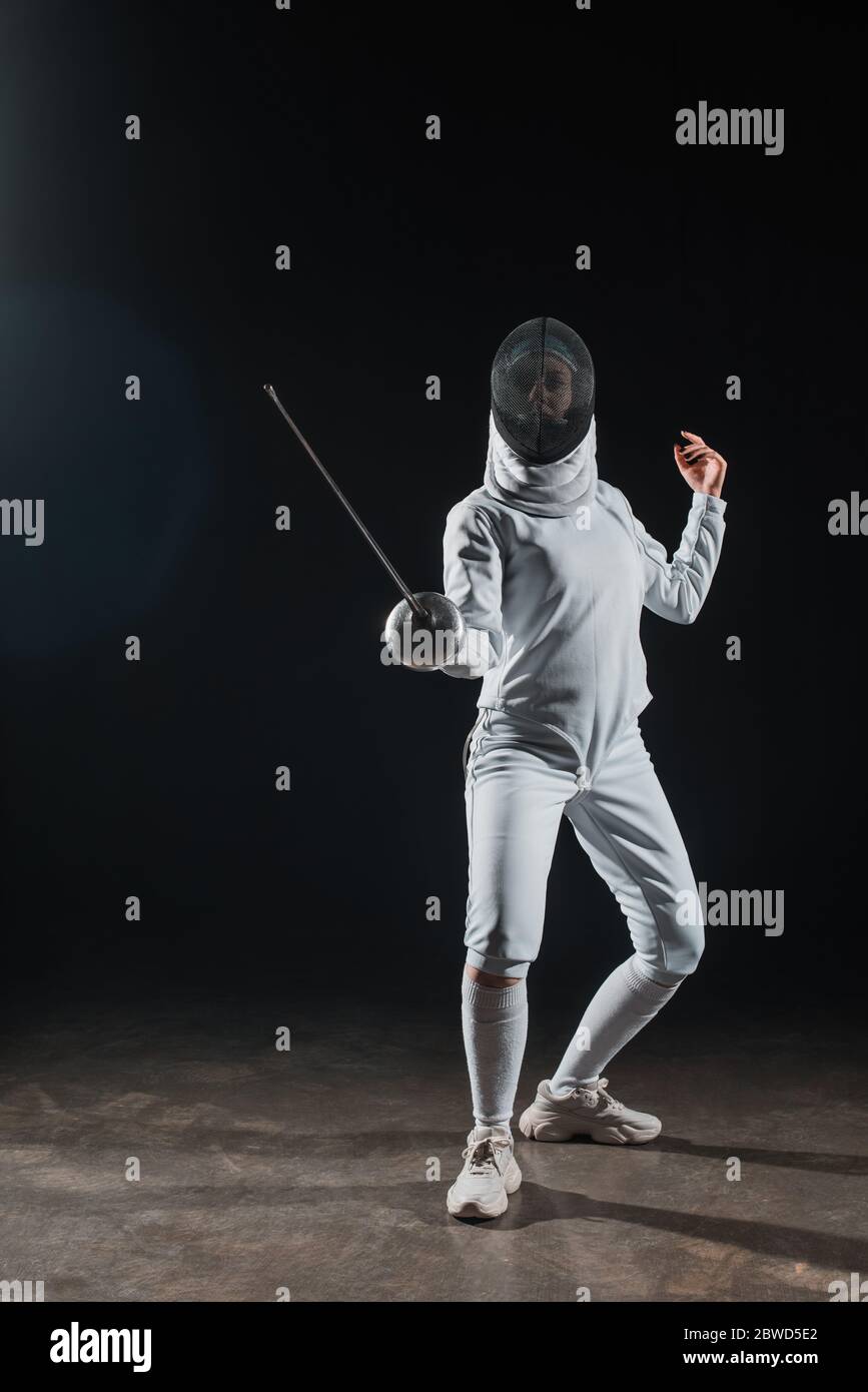 Fencer in fencing mask holding rapier while training under spotlight on ...