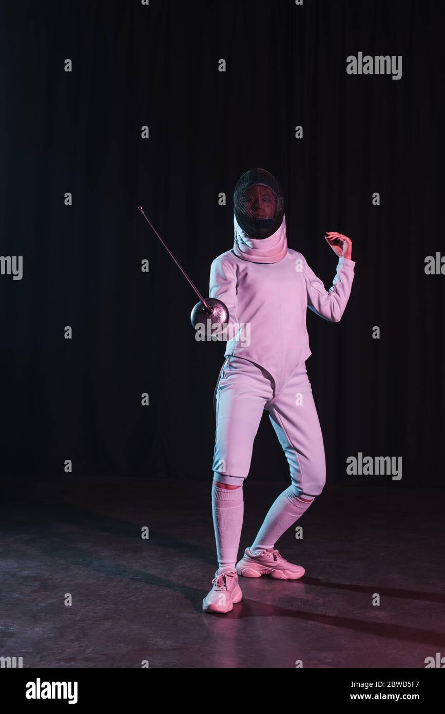 Fencer in fencing mask and suit holding rapier on black background ...