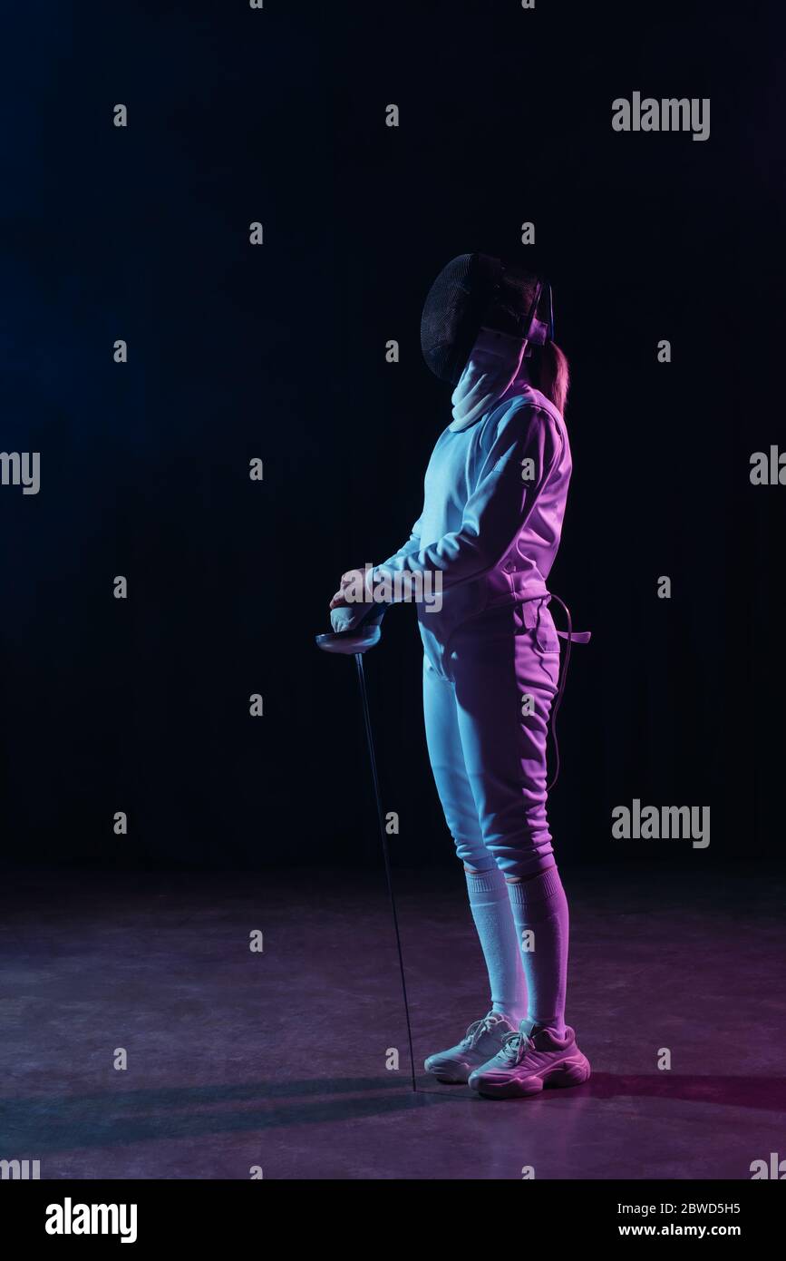 Side view of fencer holding rapier on black background with lighting ...