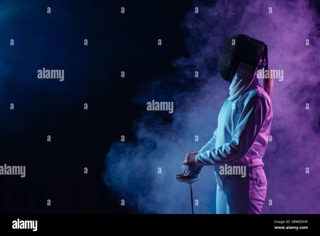 Side view of fencer in fencing mask holding rapier on black background ...