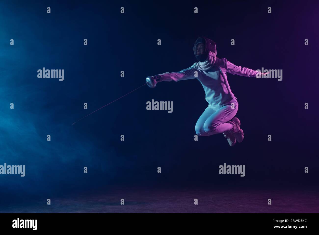 Fencer holding rapier and jumping on black background with smoke and ...