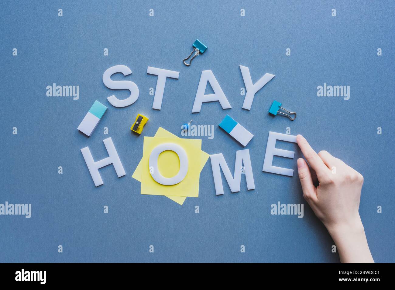 Top view of female hand near stay home lettering and stationery on blue ...
