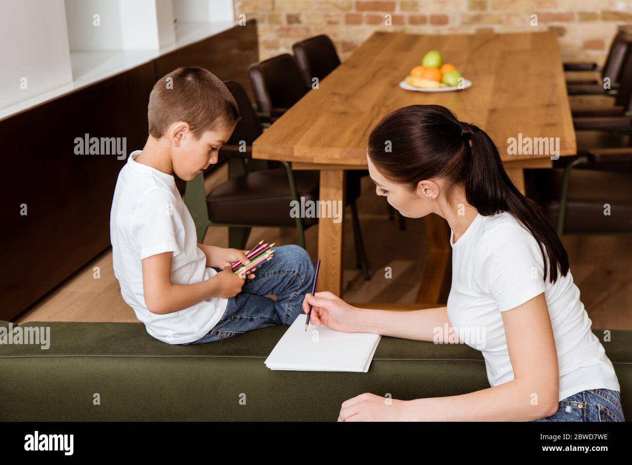 Side view of mother drawing on paper near son holding color pencils on ...