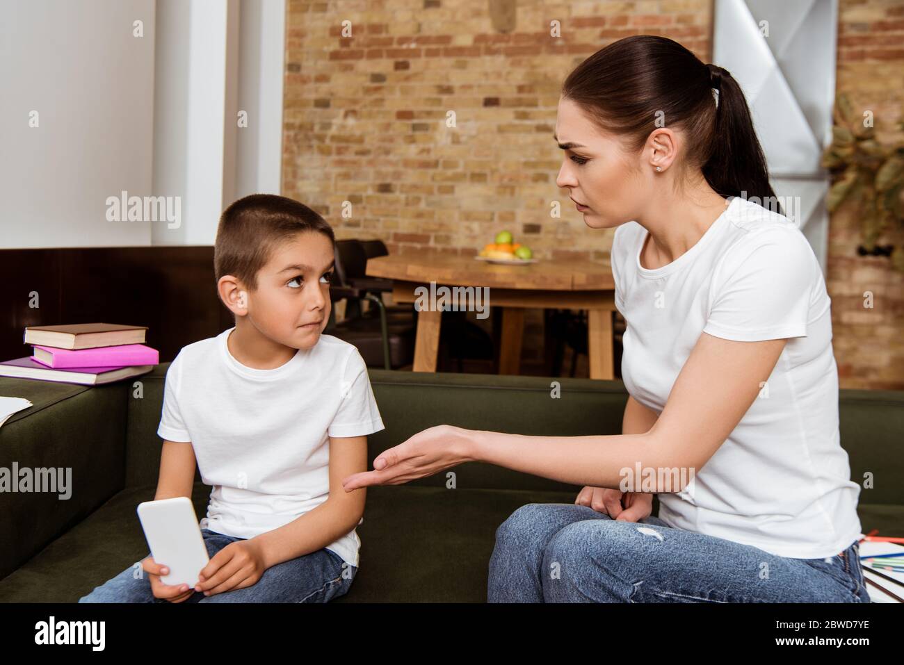 Angry mother pointing with hand at son holding smartphone on sofa Stock ...