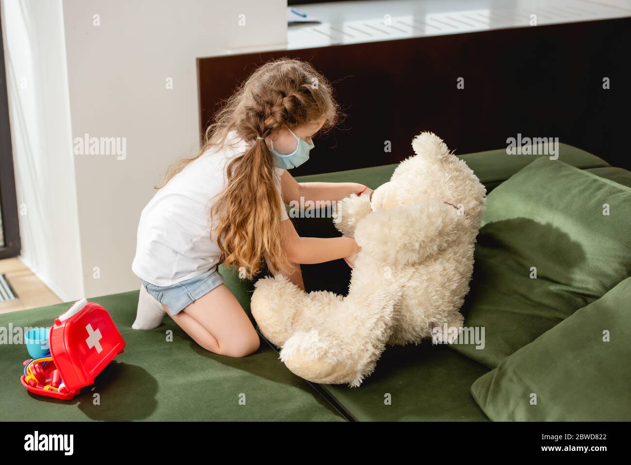 cute kid in medical mask touching teddy bear near first aid kit box ...