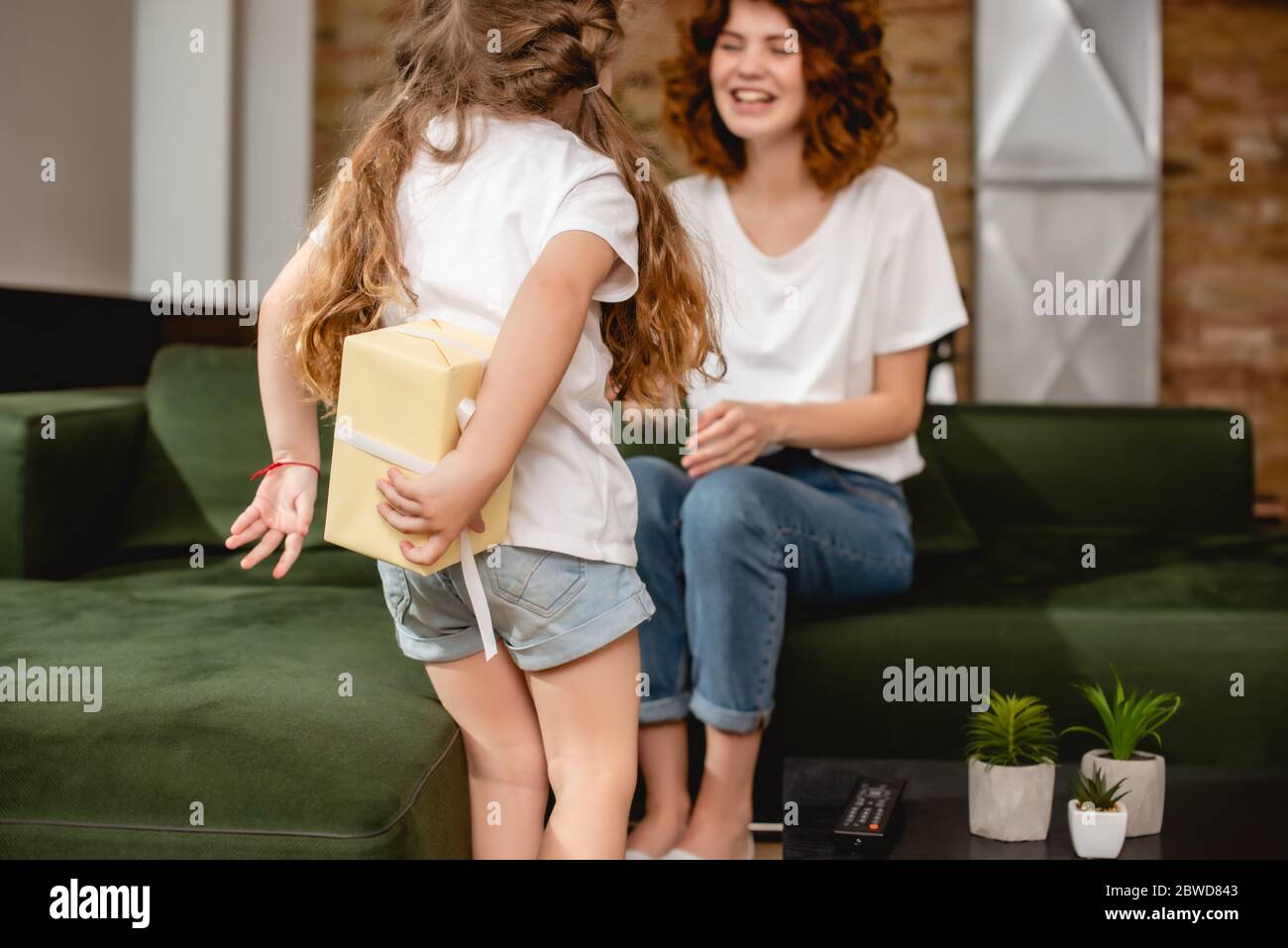 back view of kid hiding present behind back near happy mother Stock ...