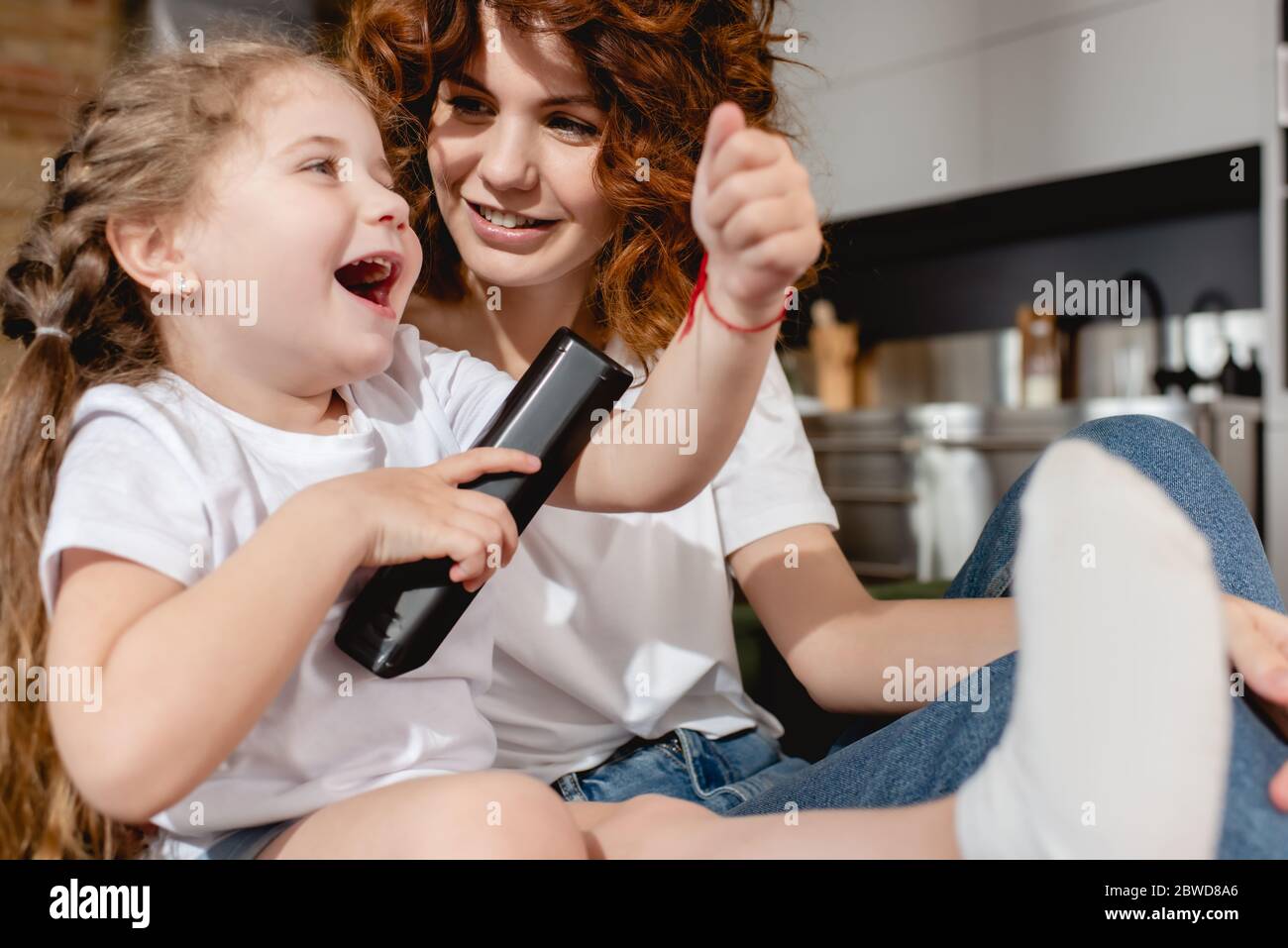 selective focus of cute kid holding remote controller near redhead ...