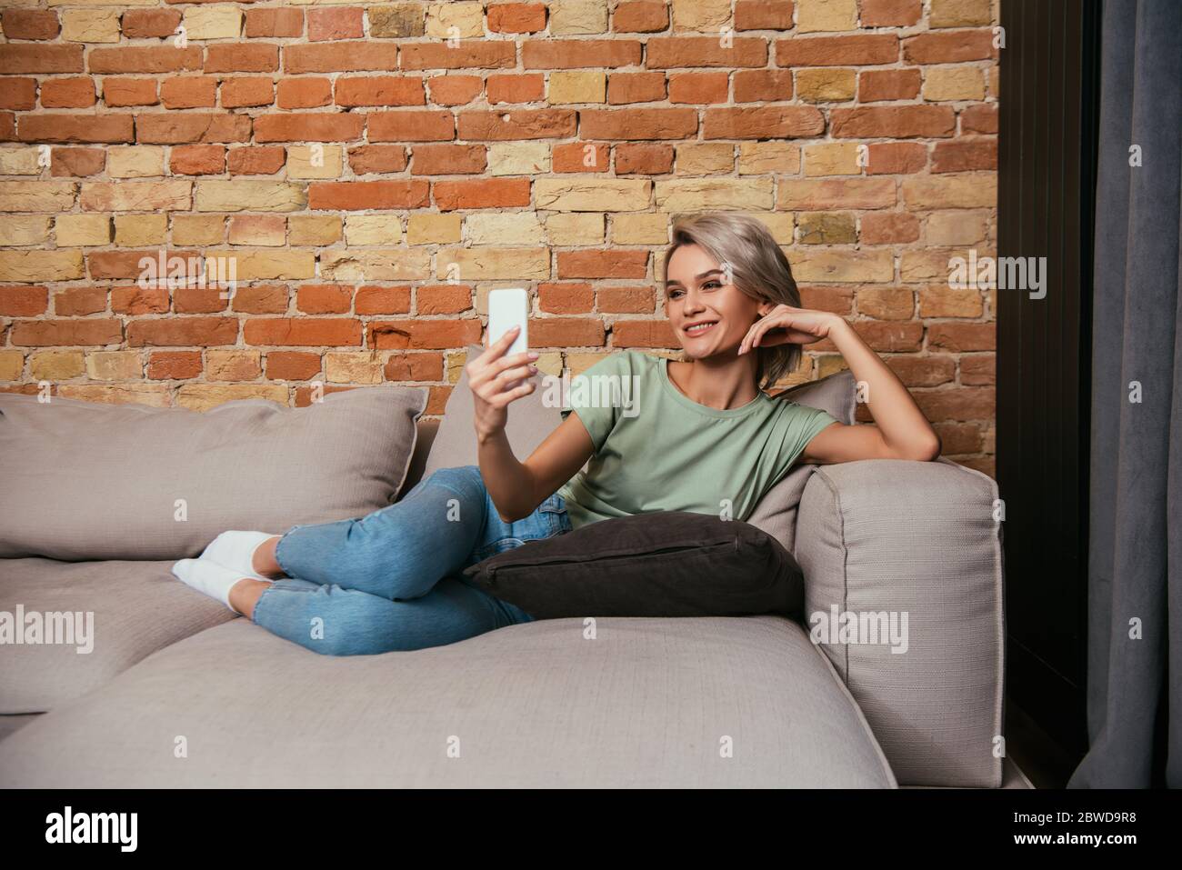 happy young woman having video chat on smartphone while relaxing on ...