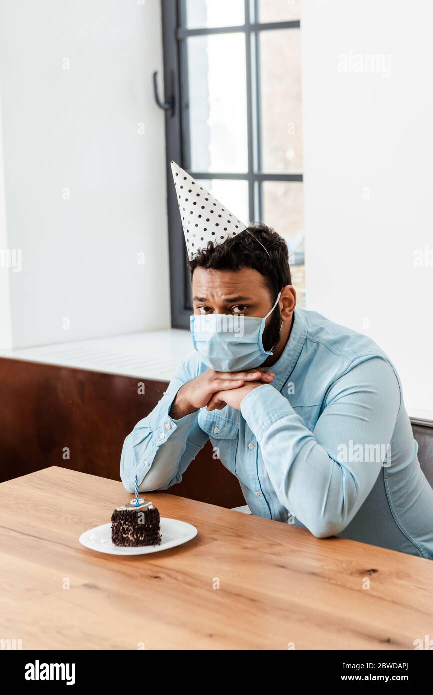 african american man in party cap and medical mask celebrating birthday ...
