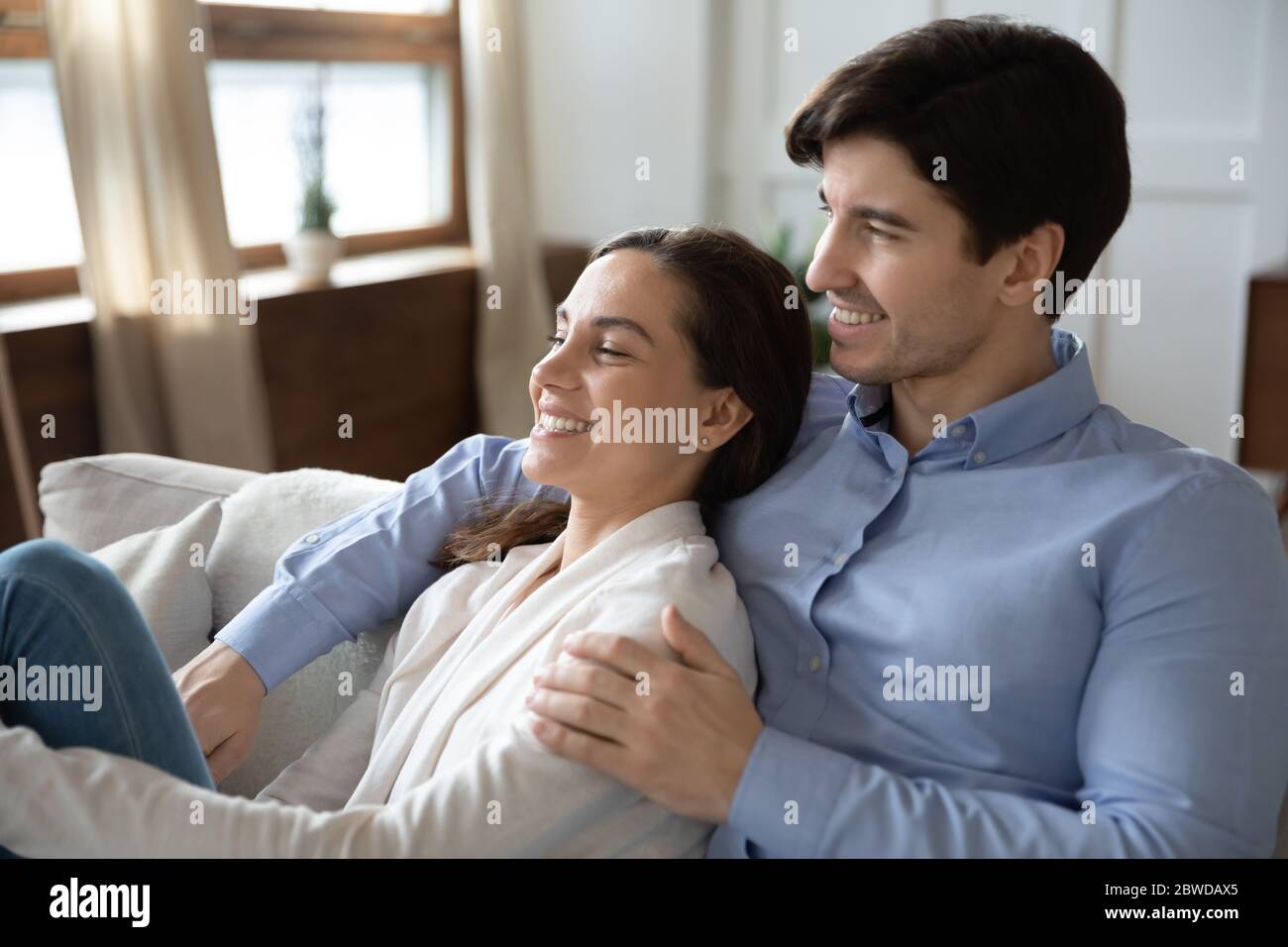 Smiling young couple relax on couch hugging Stock Photo - Alamy