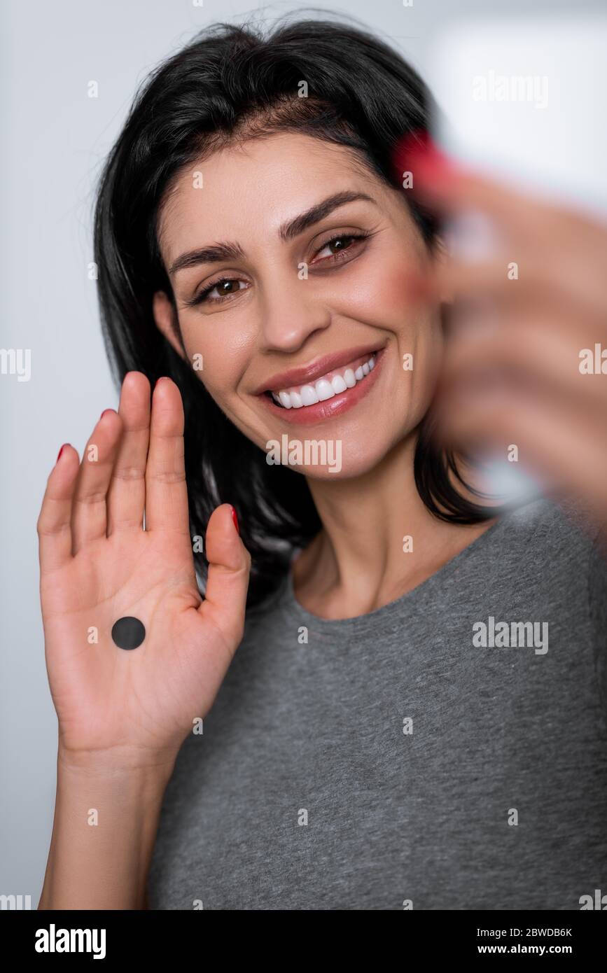 selective focus of positive woman with bruise on face and black dot on ...