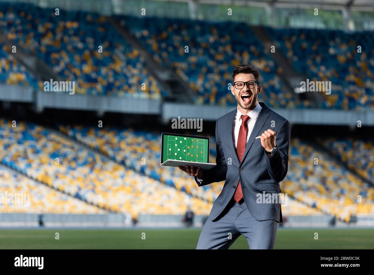 happy young businessman in suit holding laptop with football pitch and ...