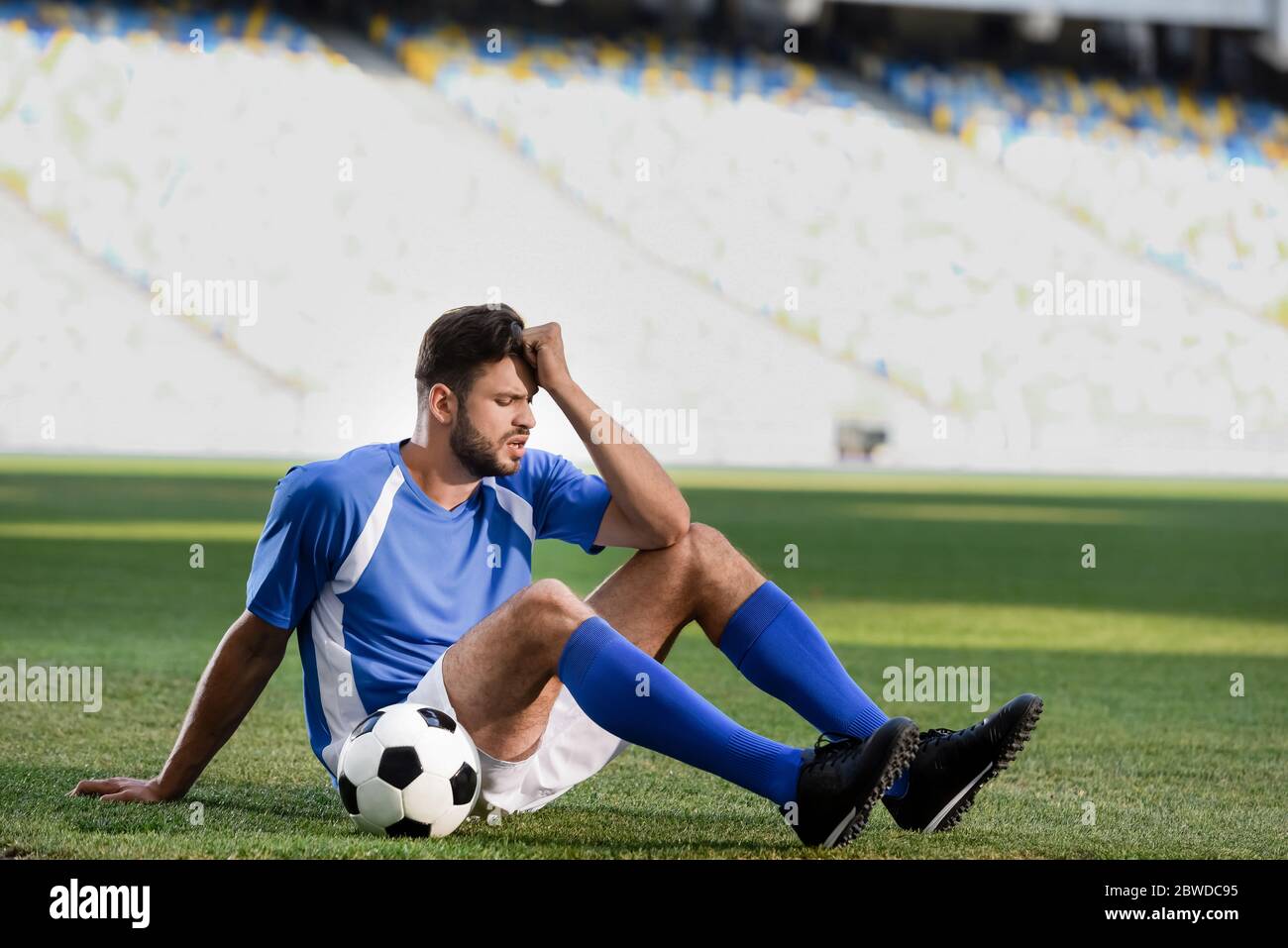 sad professional soccer player in blue and white uniform sitting with ...