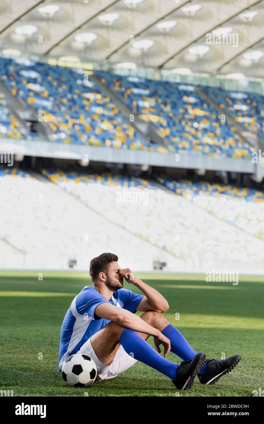 sad professional soccer player in blue and white uniform sitting with ...