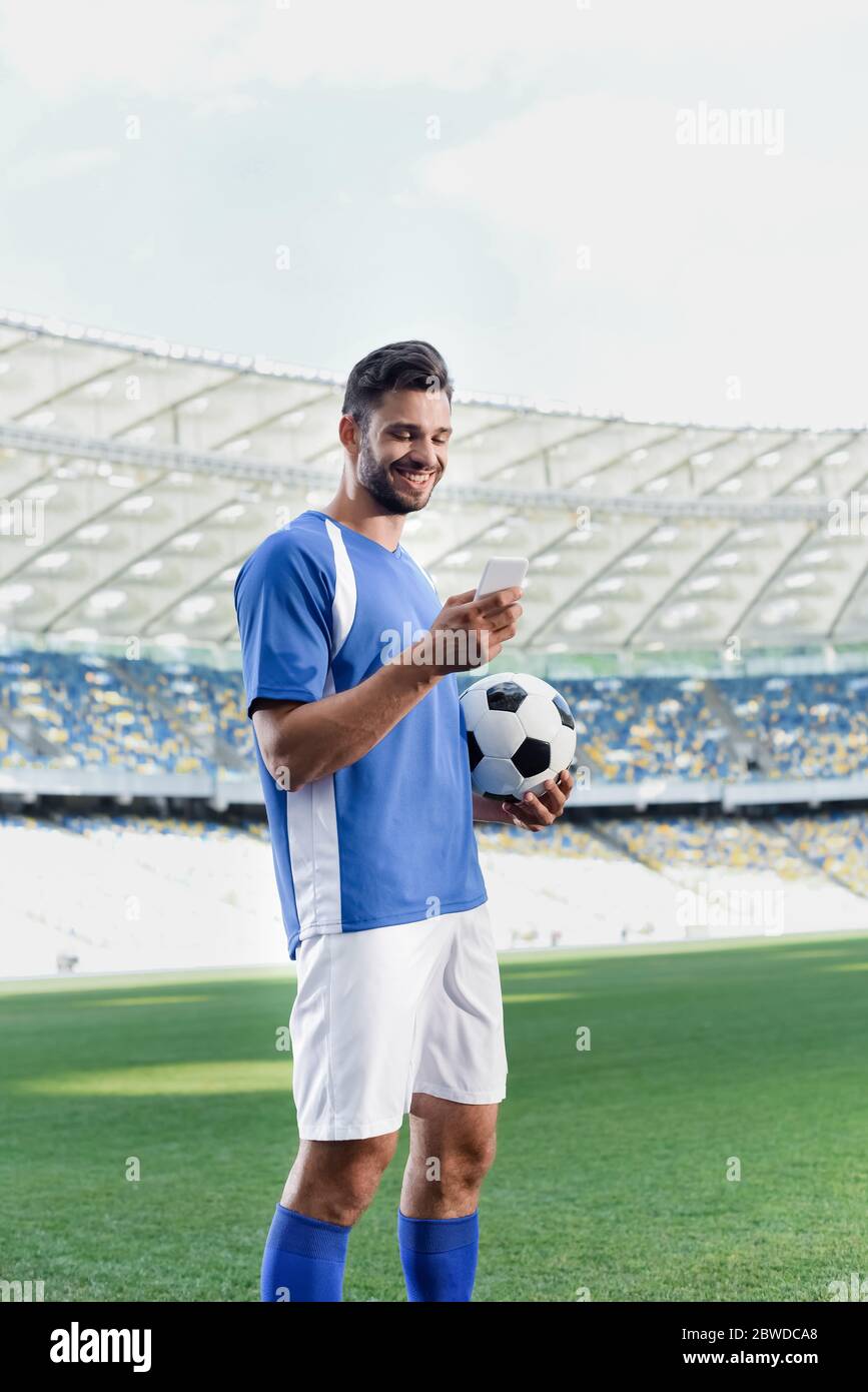 smiling professional soccer player in blue and white uniform with ball ...