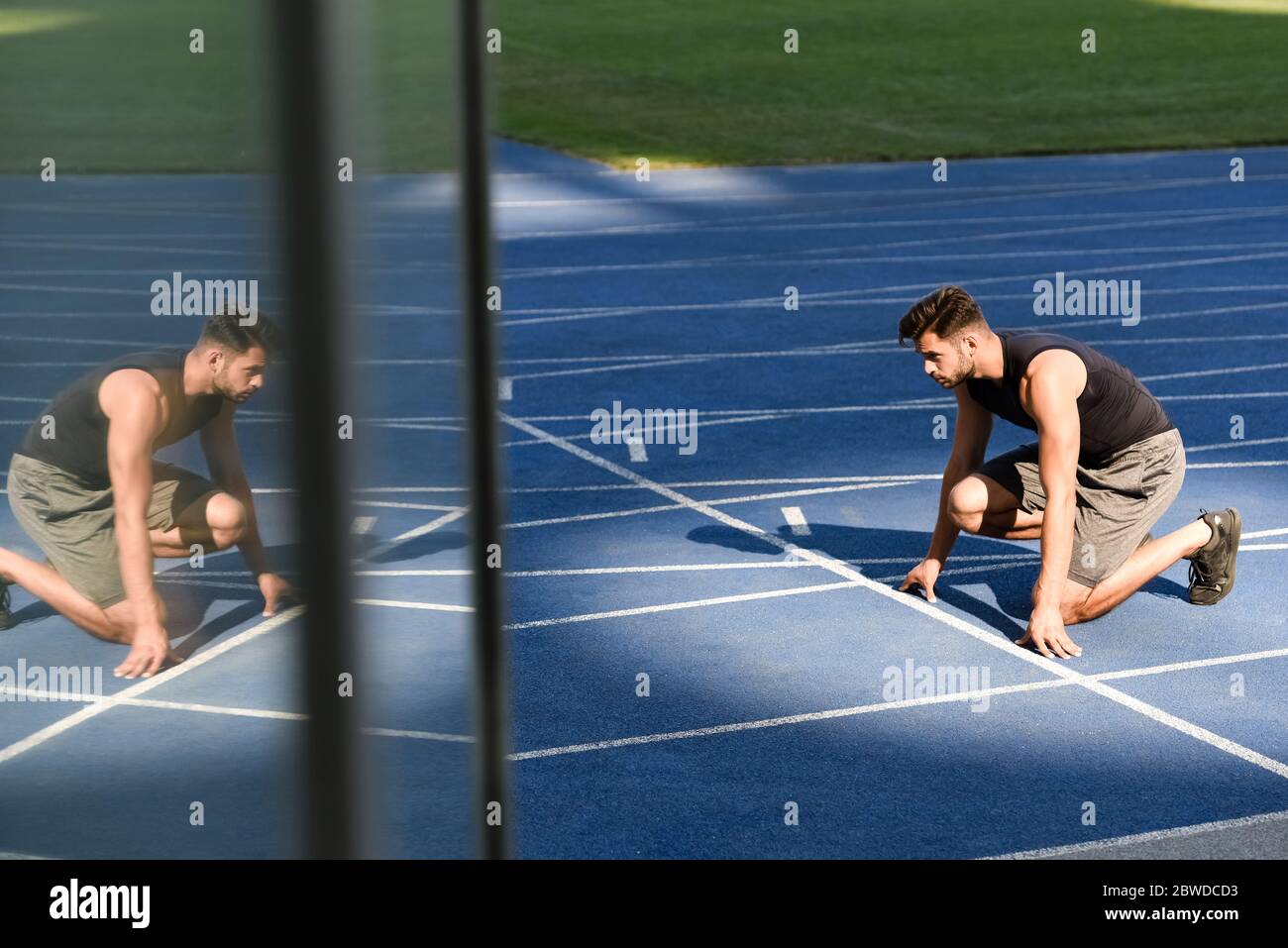 selective focus of handsome runner in start position on running track ...