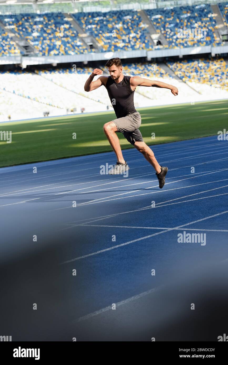 selective focus of fast handsome runner exercising on running track at ...