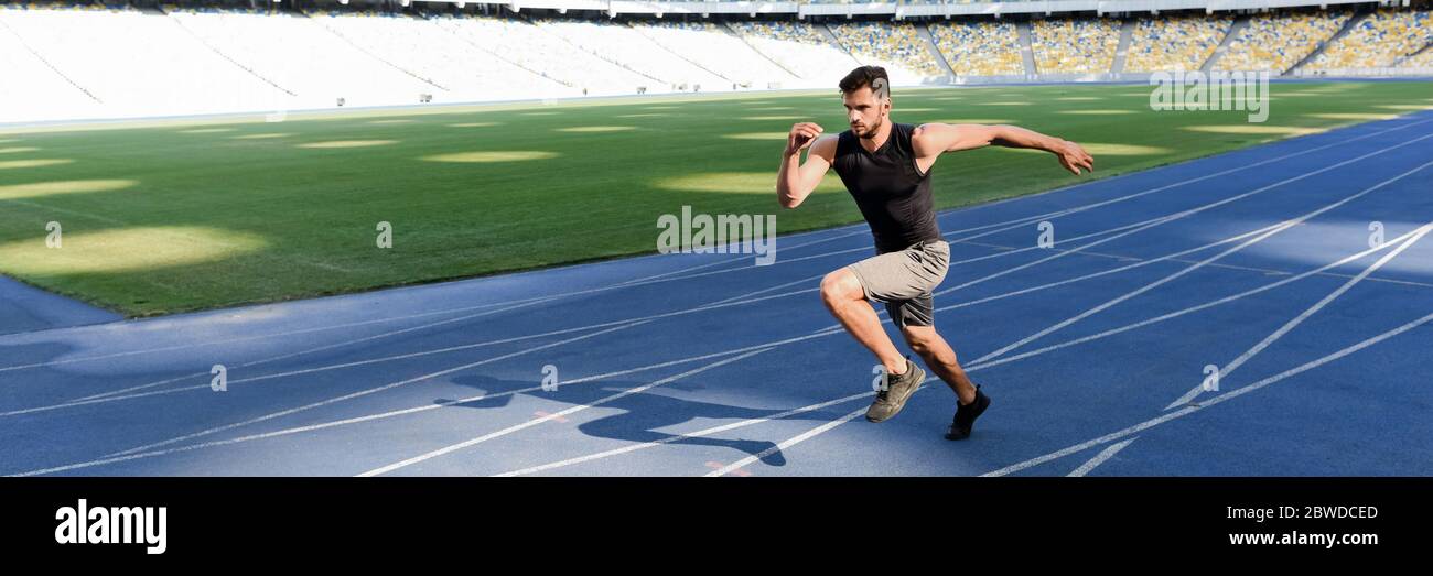handsome runner exercising on running track at stadium, panoramic shot ...