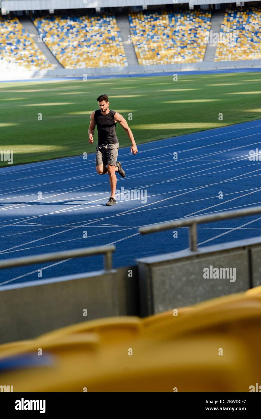 selective focus of fast handsome runner exercising on running track at ...