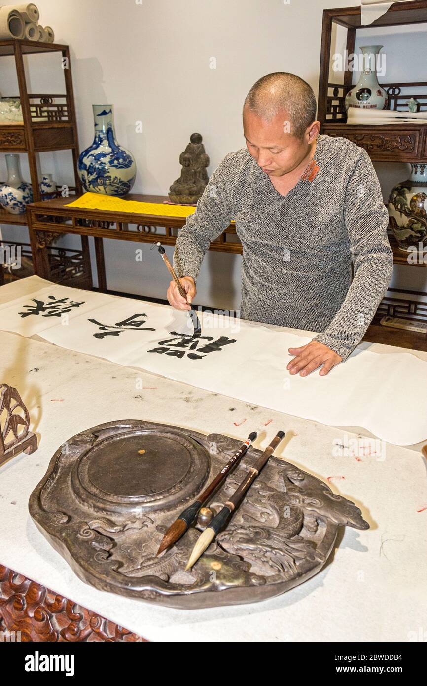 Calligrapher writing Chinese symbols on scroll at Zhen Qi Hui Art ...
