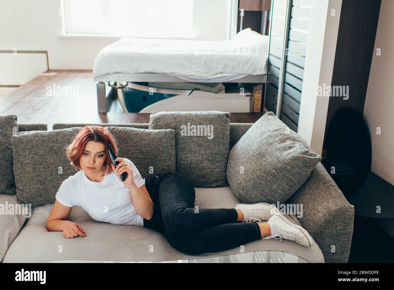 bored girl with remote controller watching tv at home on self isolation ...