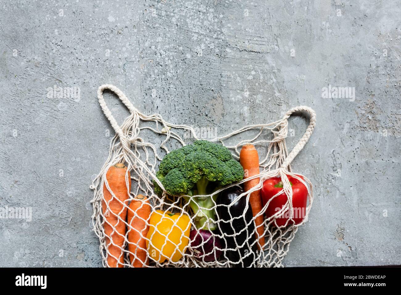 top view of fresh ripe vegetables in string bag on grey concrete ...