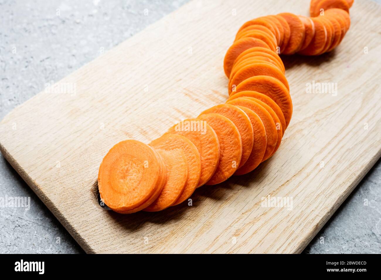 fresh ripe carrot slices on wooden cutting board on concrete surface ...