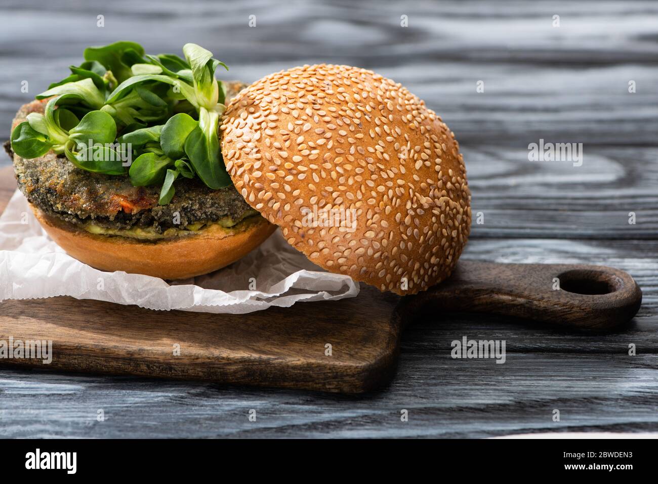 tasty vegan burger with microgreens served on cutting board on wooden ...